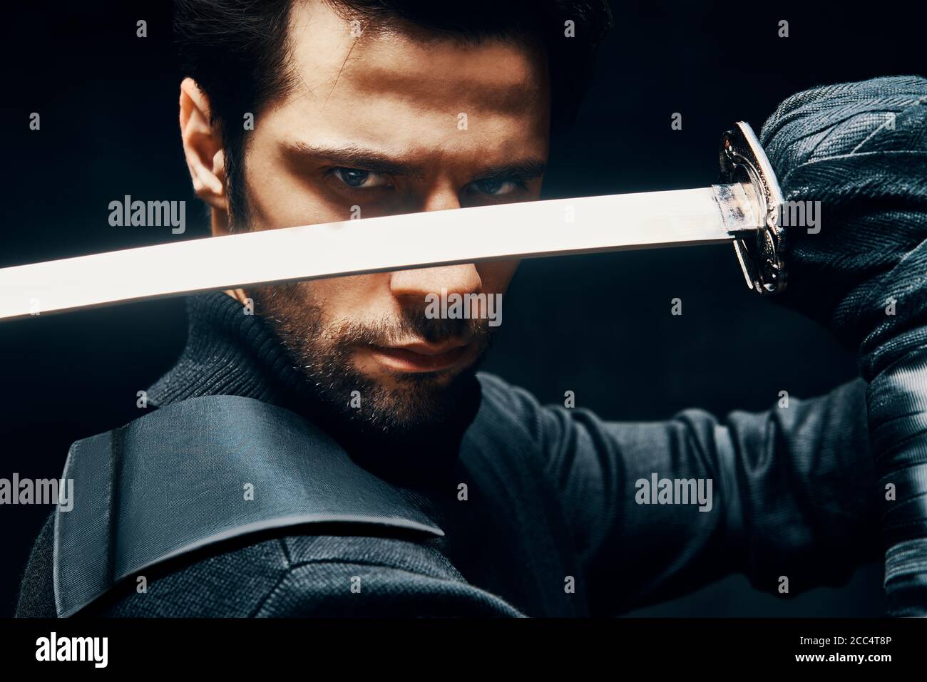 Warrior man posing with a sword isolated on black background. Close up ...
