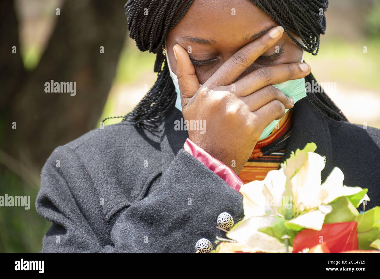 Young black woman mourning, wearing a mask and holding flowers - the ...