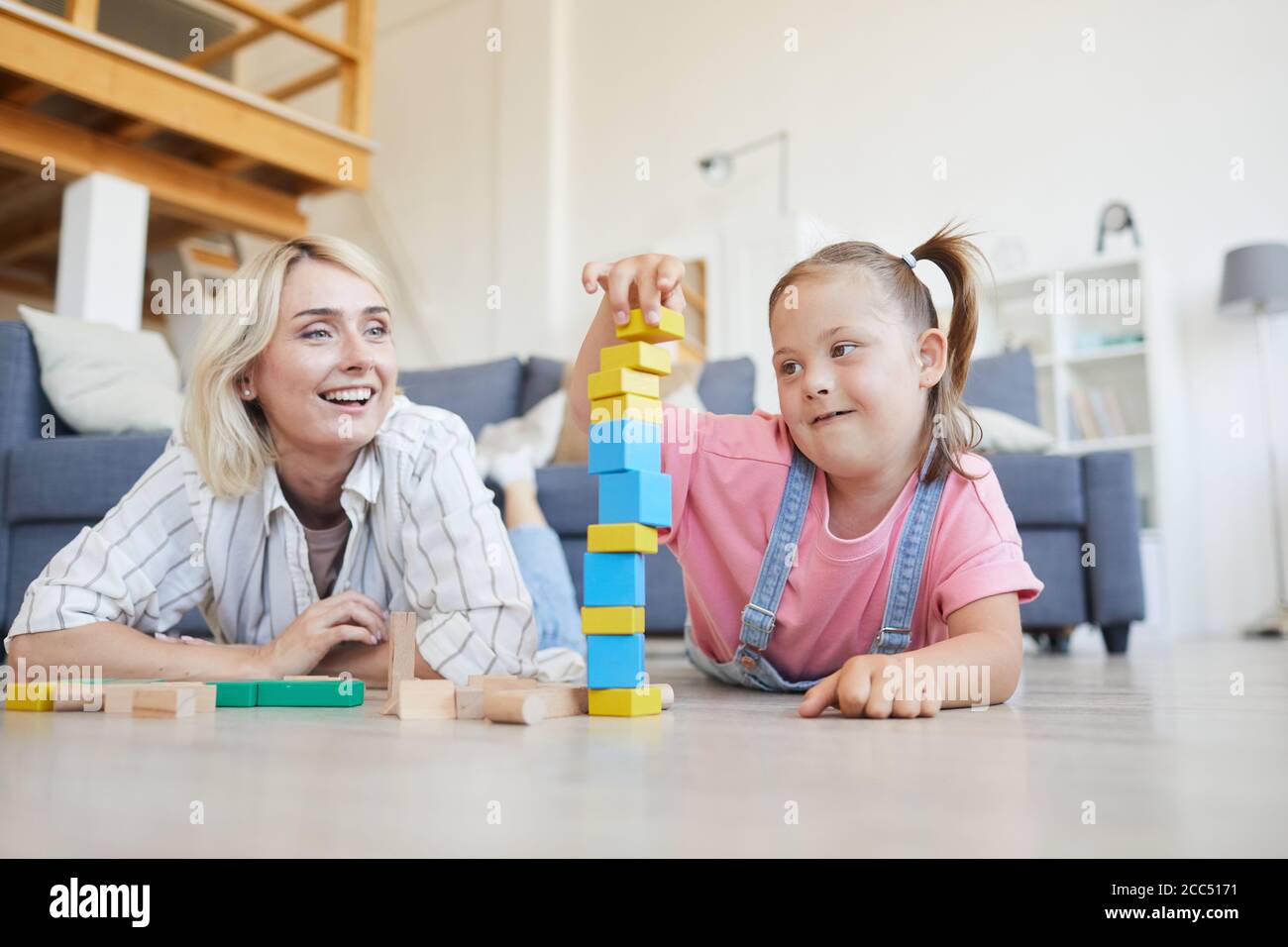 Little girl with down syndrome building a tower from colored blocks ...