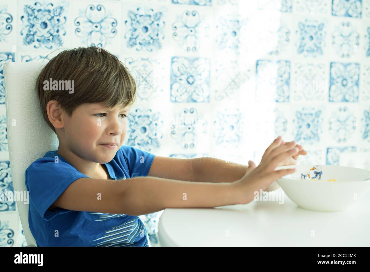 a boy in a blue T-shirt has breakfast with oatmeal and milk in a white ...