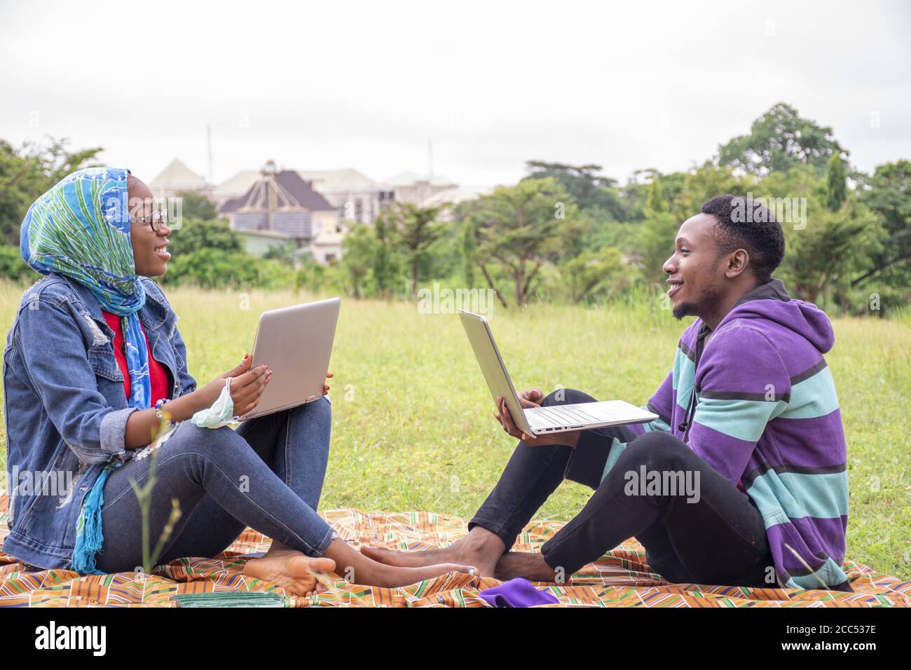 Shallow focus of two young African people using their laptops at a park ...