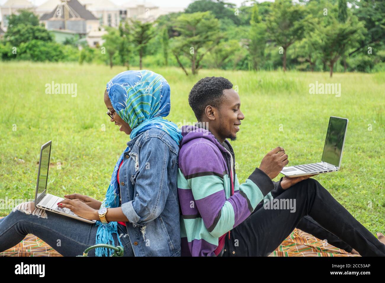 Shallow focus of two young African people using their laptops at a park ...