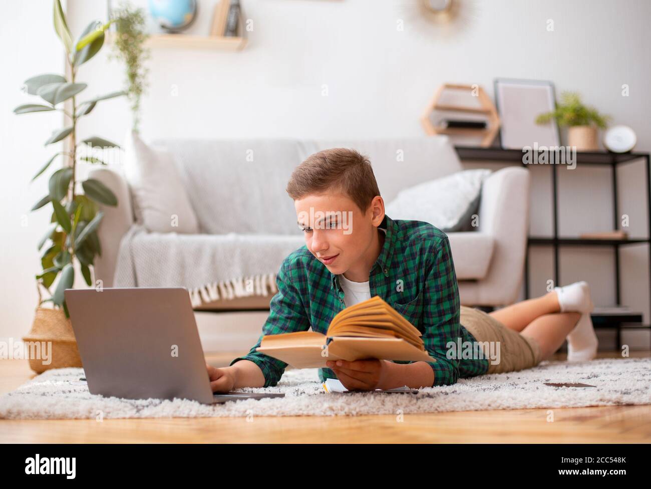 Cheerful teen boy reading book and typing on laptop Stock Photo - Alamy