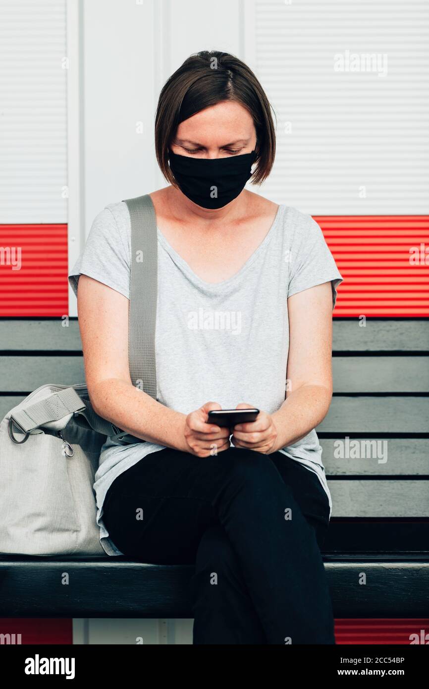 Woman with protective face mask typing text message on smartphone while ...