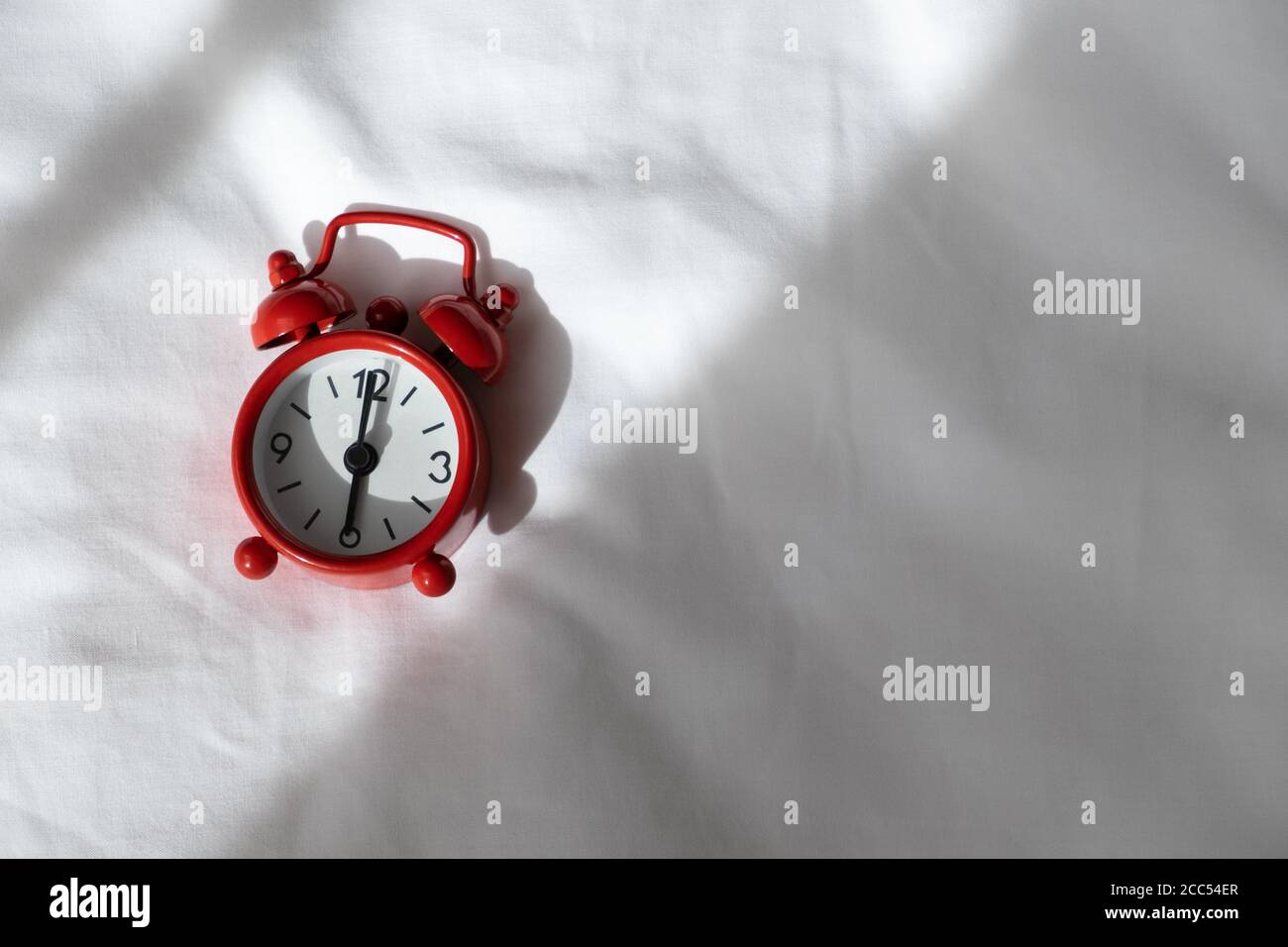 Red analog clock on white rumpled sheets. Top view, flat lay, copy ...
