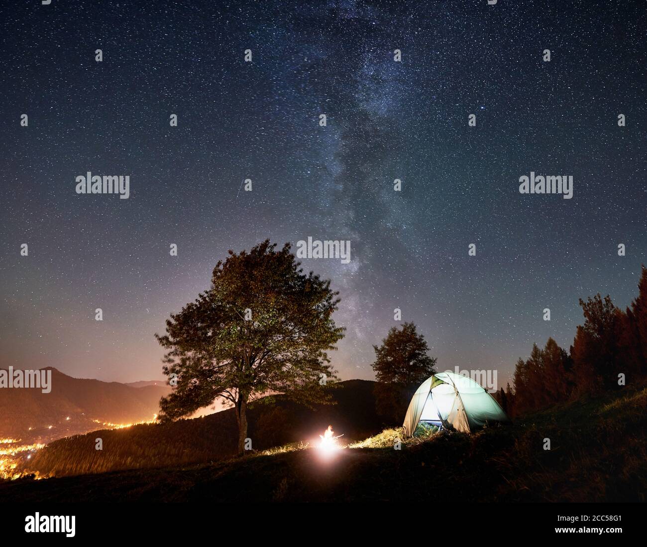 Tourist camping near forest at summer night. Glowing tent and campfire ...