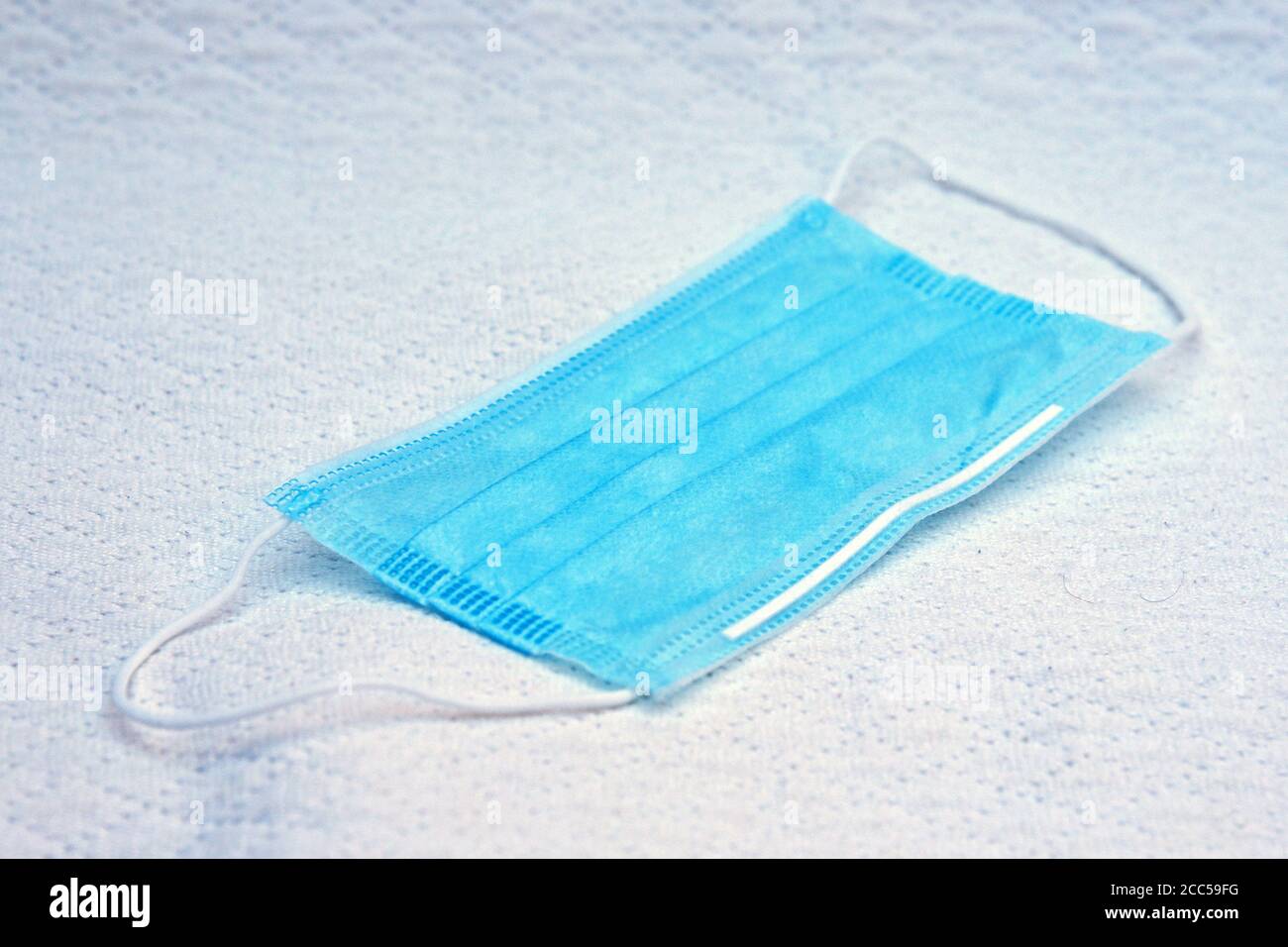 A single disposable surgical face mask on white textile background ...