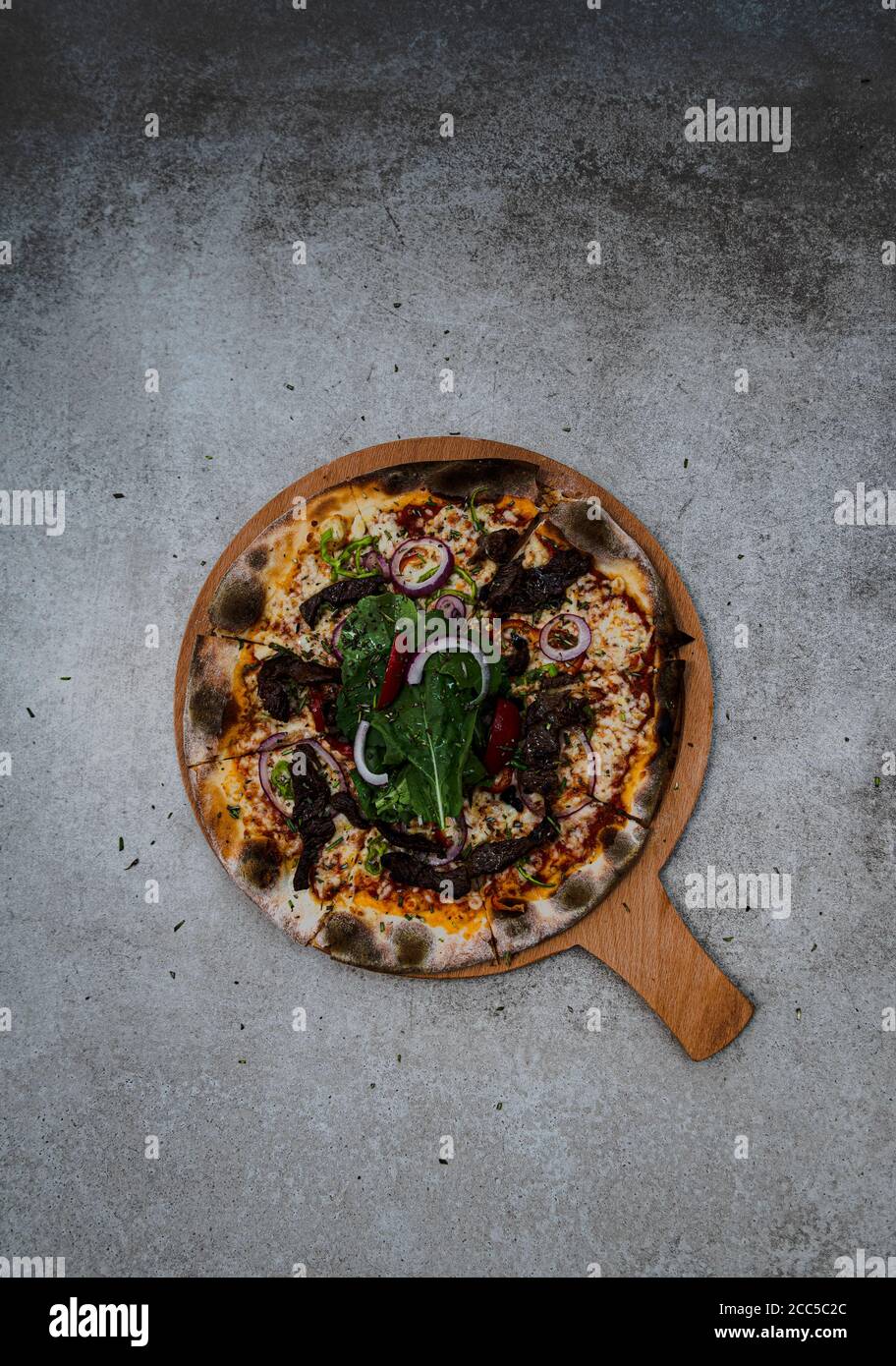 Vertical high angle shot of a delicious pizza on a wooden plate on a ...