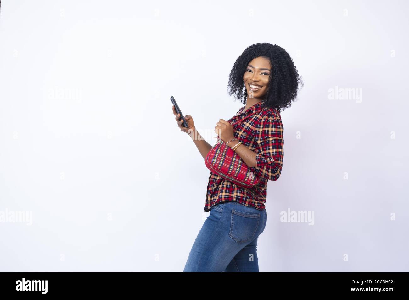 Excited young African lady standing sideways using her phone Stock ...