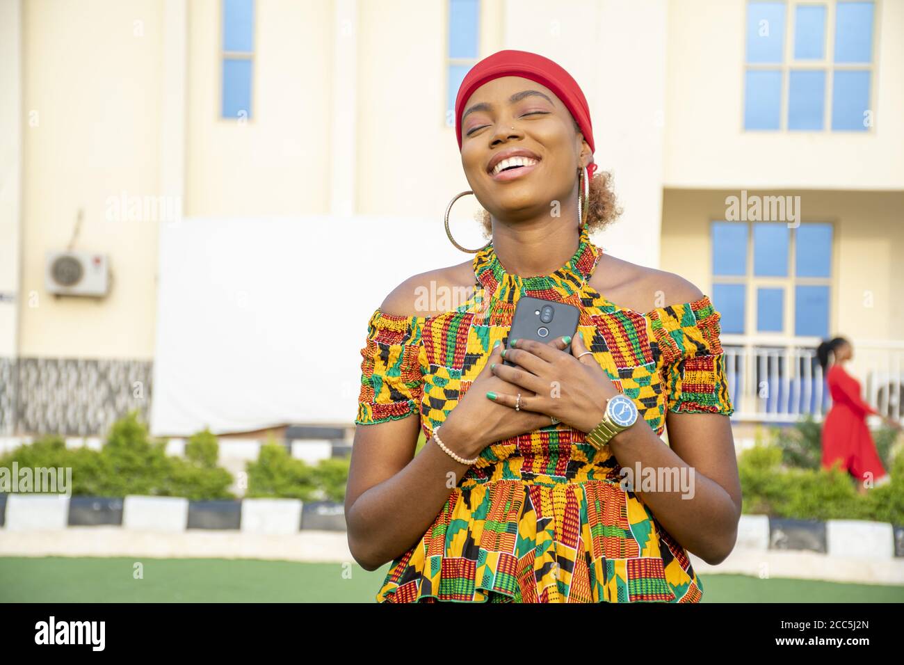 Beautiful African lady holding her phone to her chest filled with joy ...