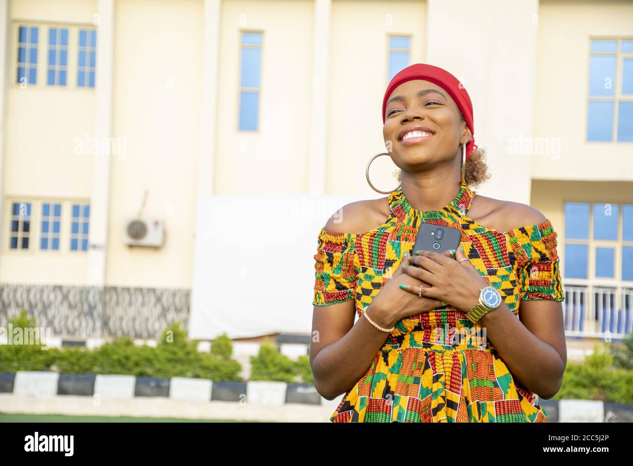 Beautiful African lady holding her phone to her chest filled with joy ...