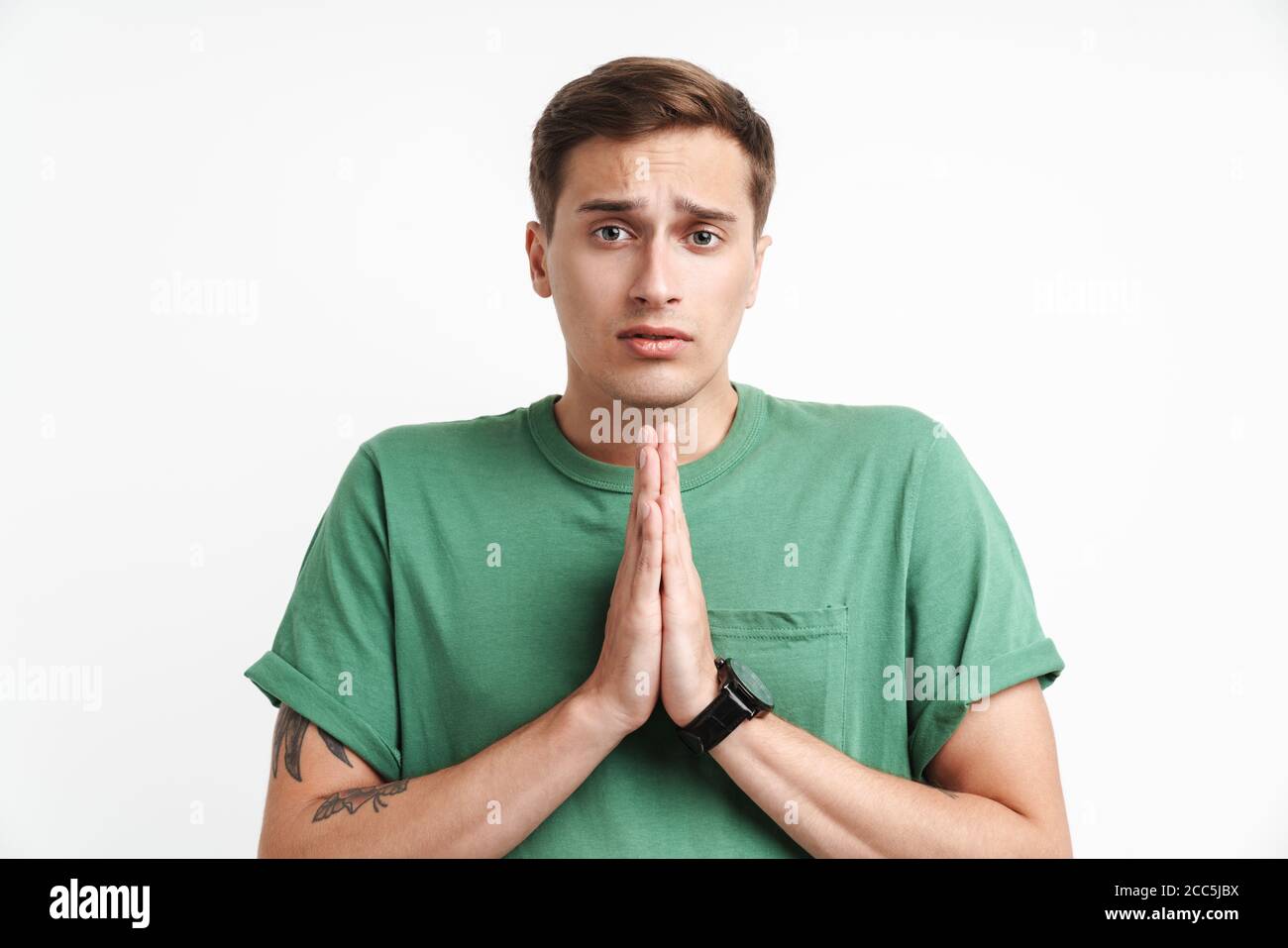 Image of uptight caucasian man in basic t-shirt praying and holding ...