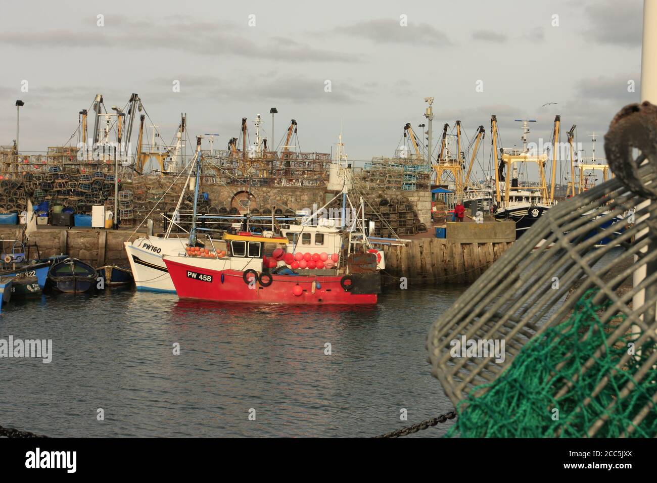 Fishing boats moored alongside quay with crab pots on the quayside ...