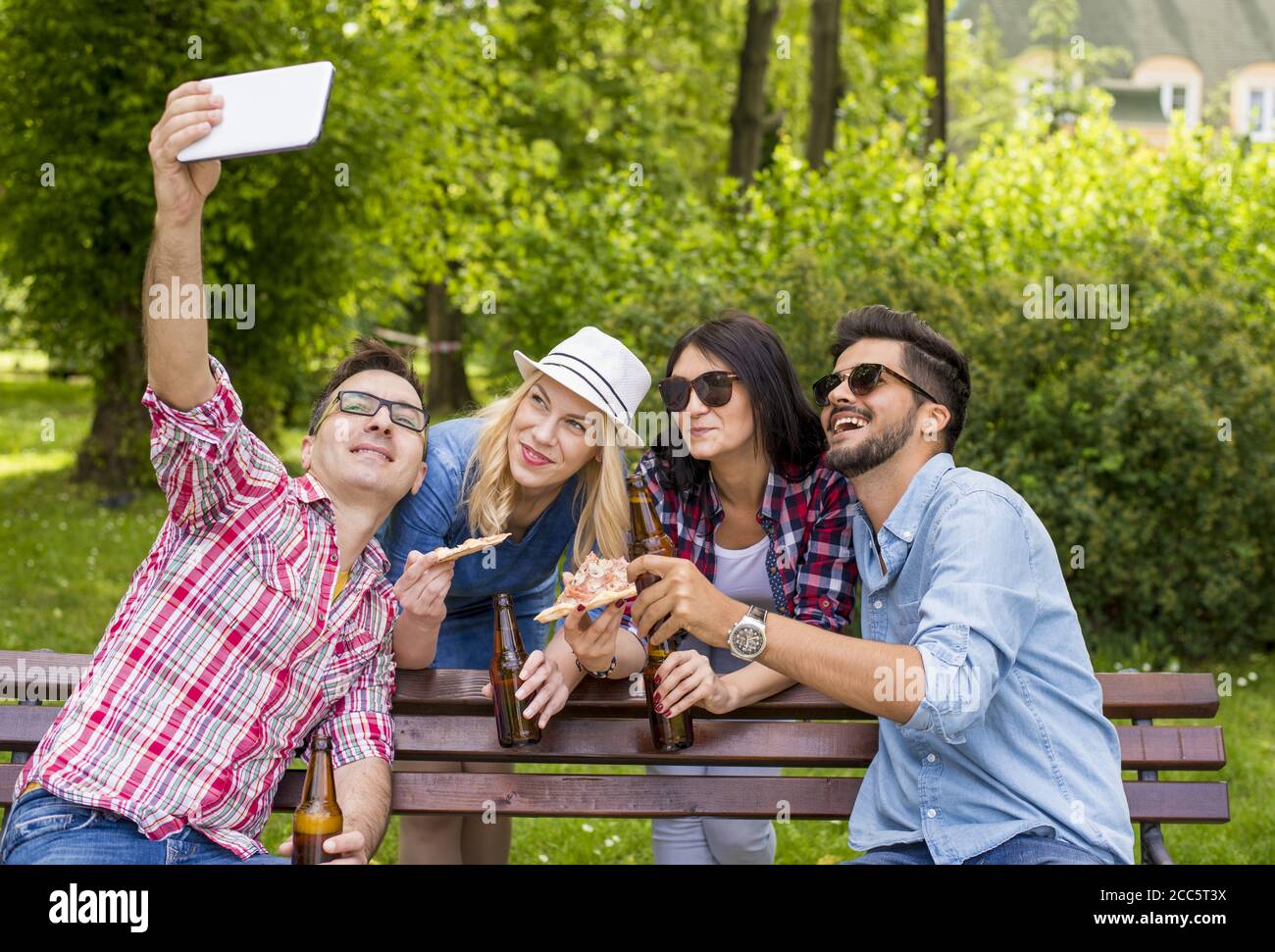 Group of friends sitting on a bench drinking beer and taking selfies ...