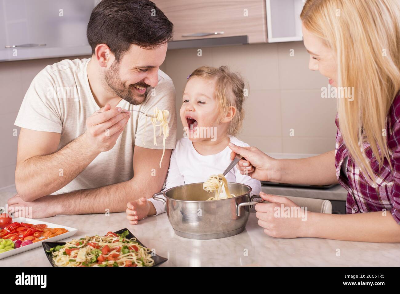 Happy family and their young daughter eating spaghetti on the kitchen ...