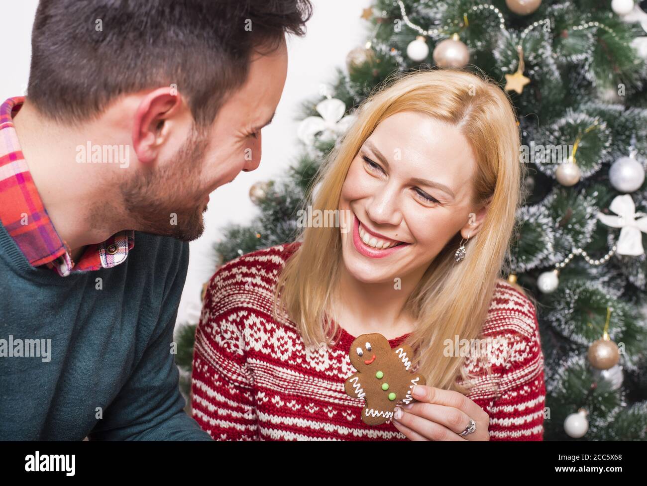 Laughing couple holding gingerbread man on background of Christmas tree ...