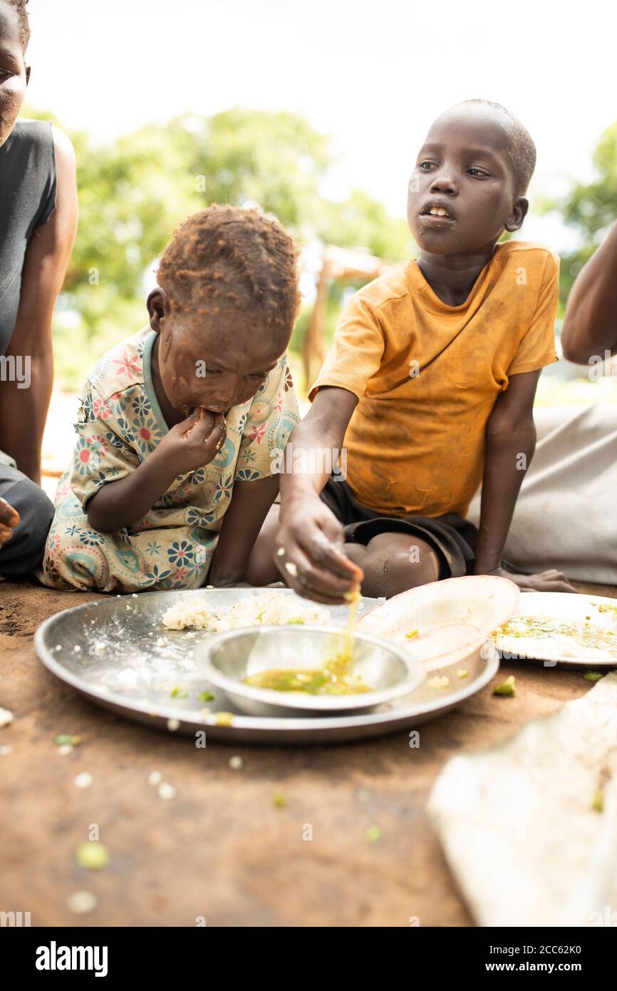 Two children eat a meal together at Palabek Refugee Settlement in ...