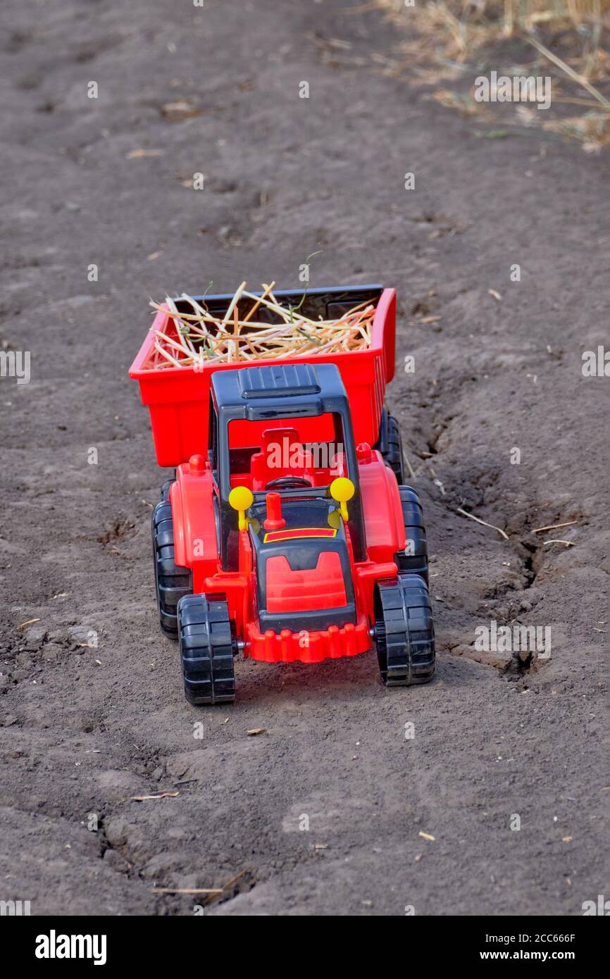 A red toy tractor with a trailer on a road in a real agricultural field ...