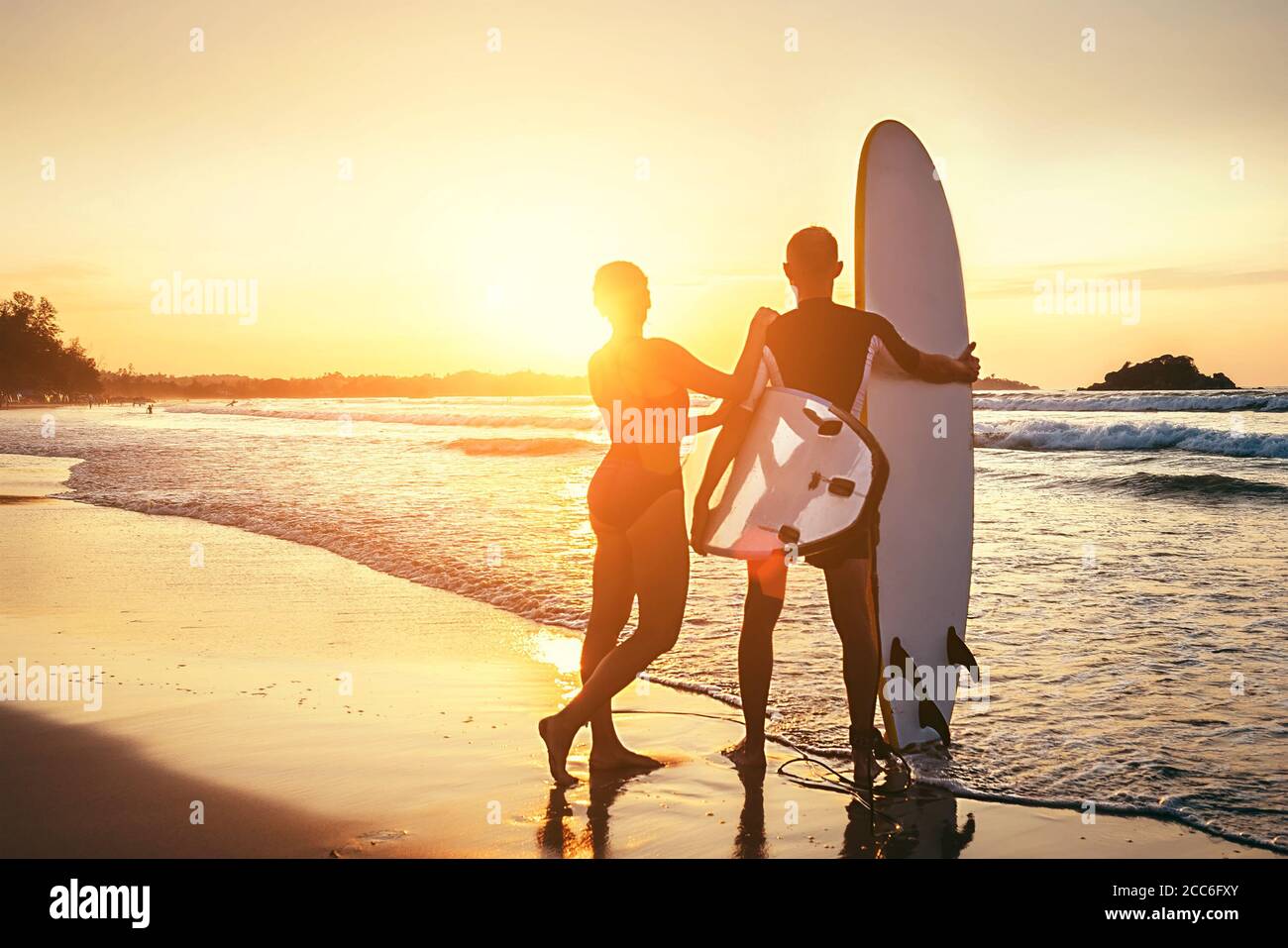 Couple surfers stay on sunset ocean beach Stock Photo - Alamy