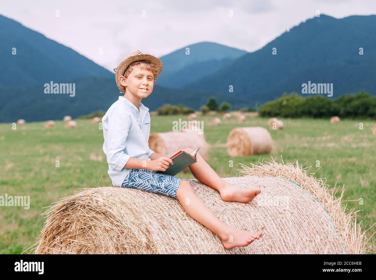 Reading boy sits over the haystack roll on the mountain field Stock ...