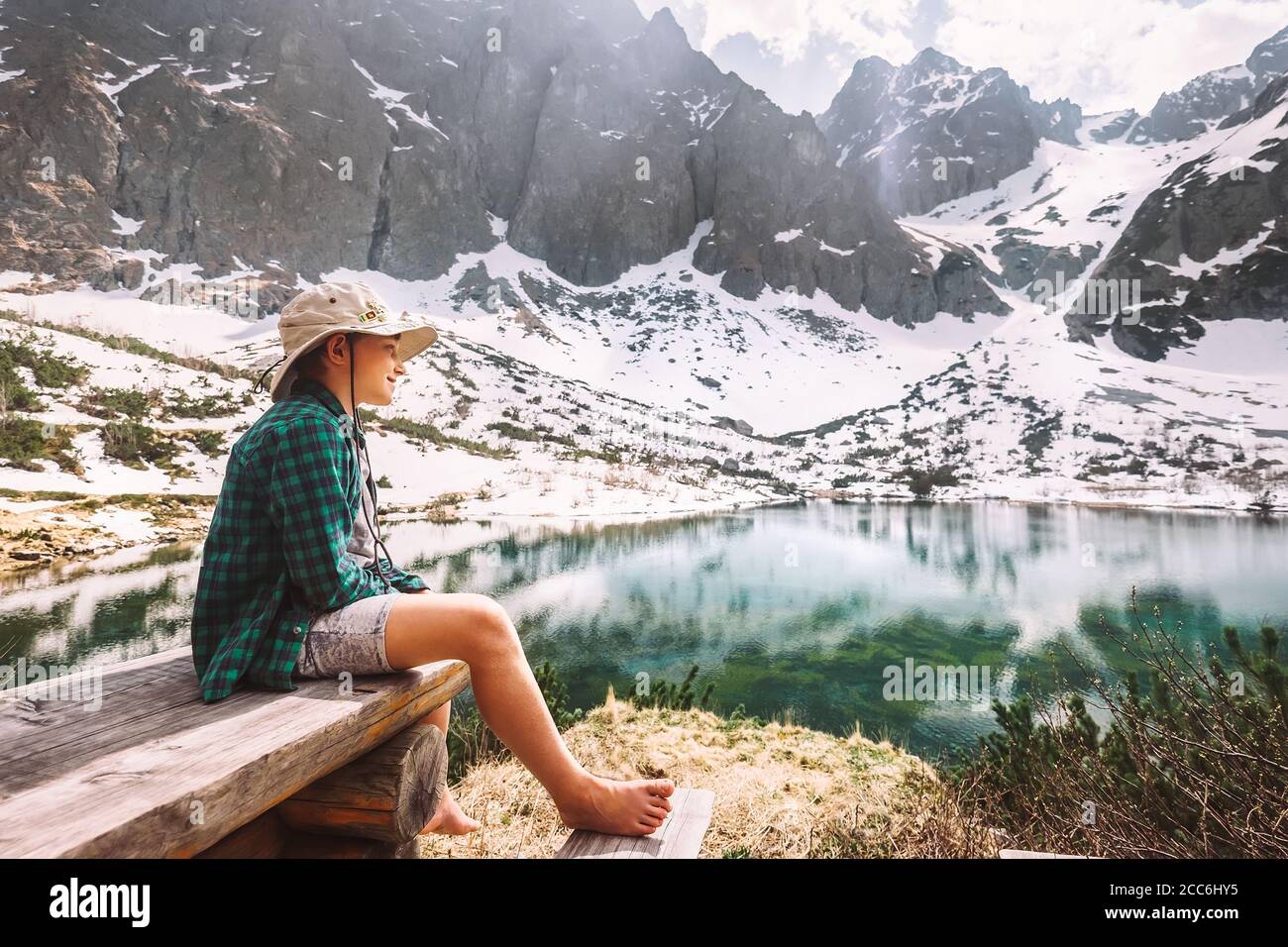 Boy traveler rest after hiking near mountain lake around snowy peaks ...