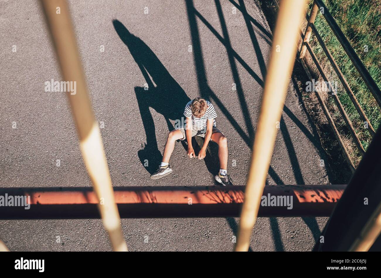 An alone boy without friends sits on a skateboard. Child loneliness ...