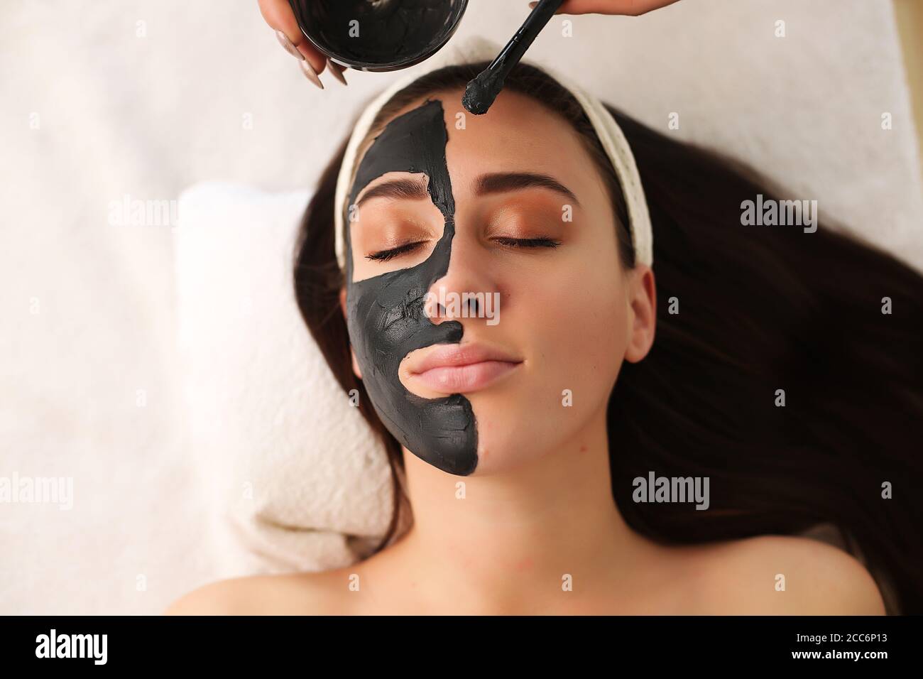 Cosmetologist smears cosmetic mask on the face of the woman in the sap ...