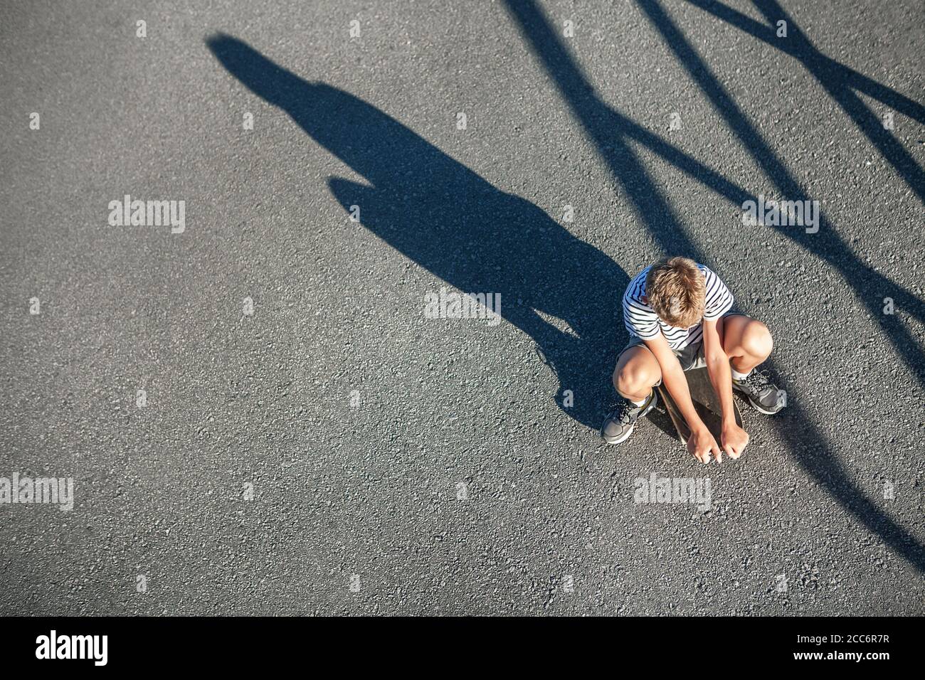An alone boy without friends sits on a skateboard. Child loneliness ...