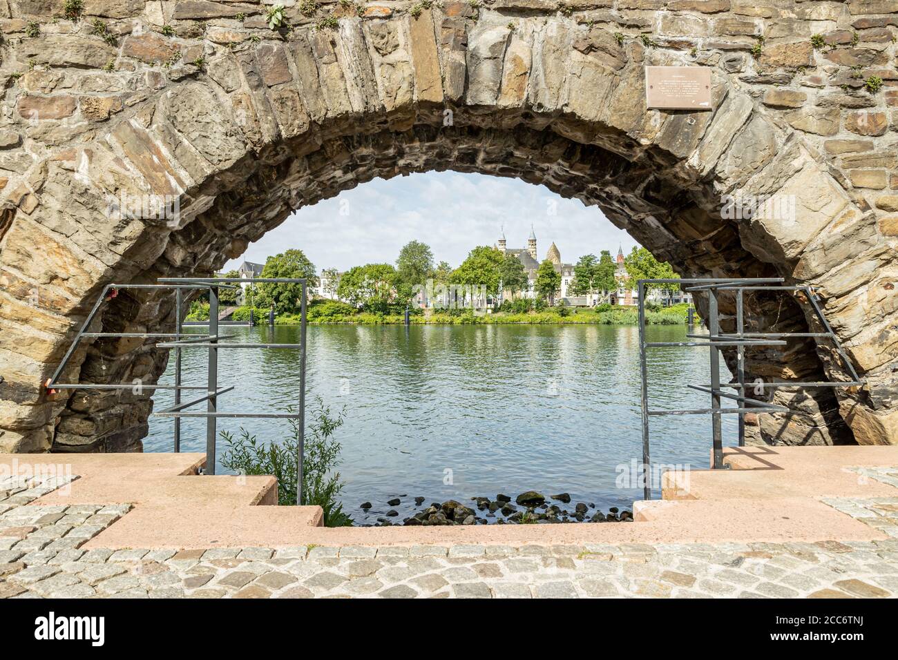 Stone arch of an old medieval city wall with the Maas river and ...