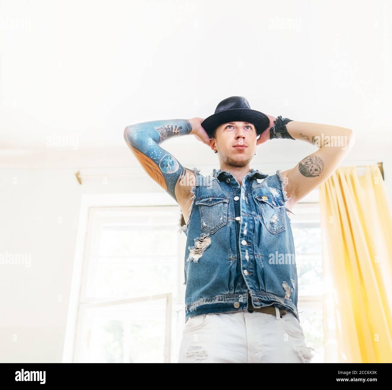 Modern tattooed art dancer dressed in jeans vest and black hat posing ...
