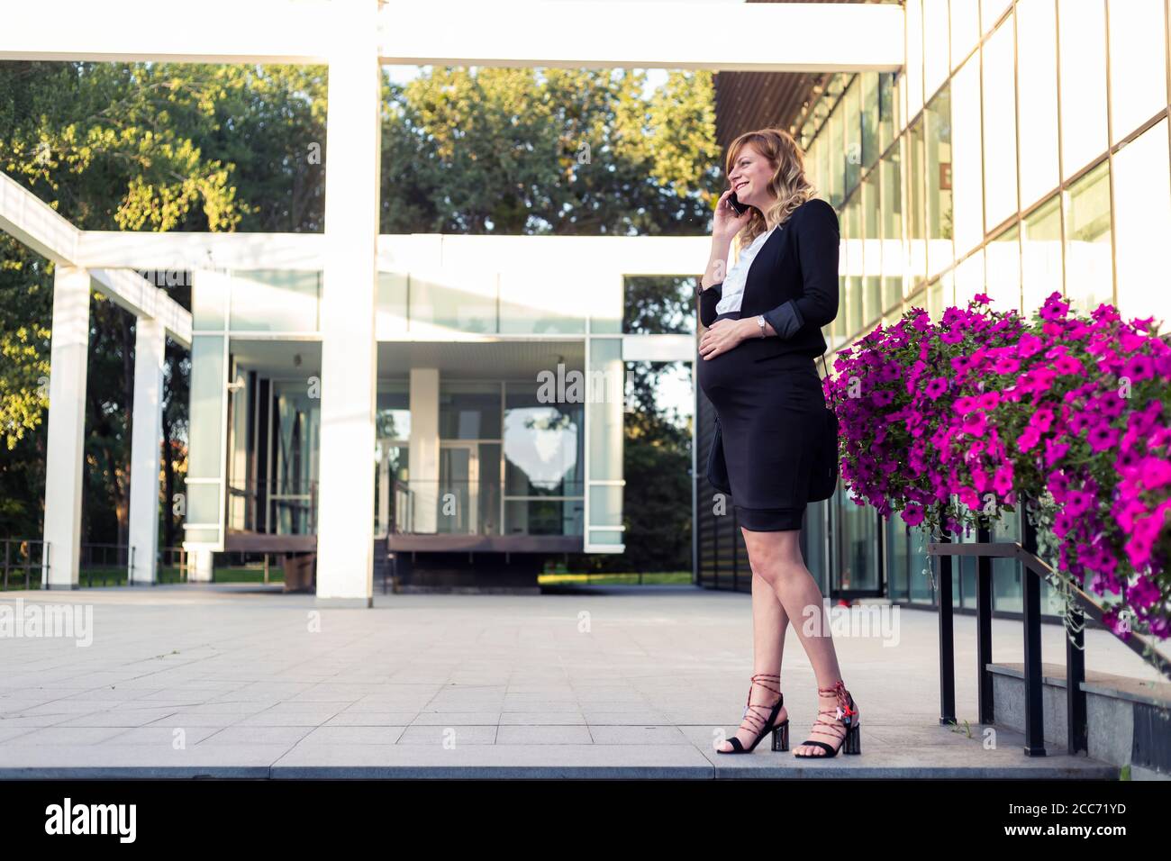 A smiling pregnant businesswoman standing beside flowers in front of a ...