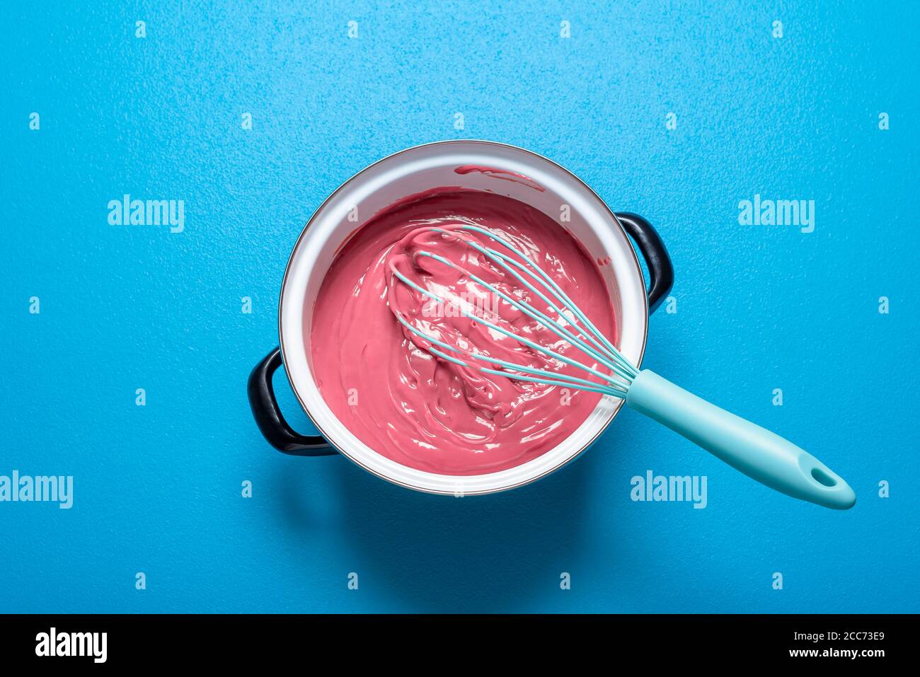 Melted Ruby chocolate in a pot, isolated on a blue background. Top view ...