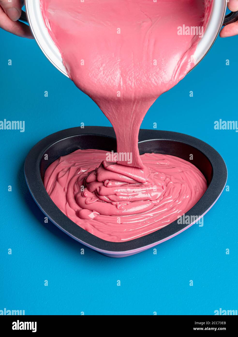 Melted ruby chocolate pour into a heart shape mold on a blue background ...