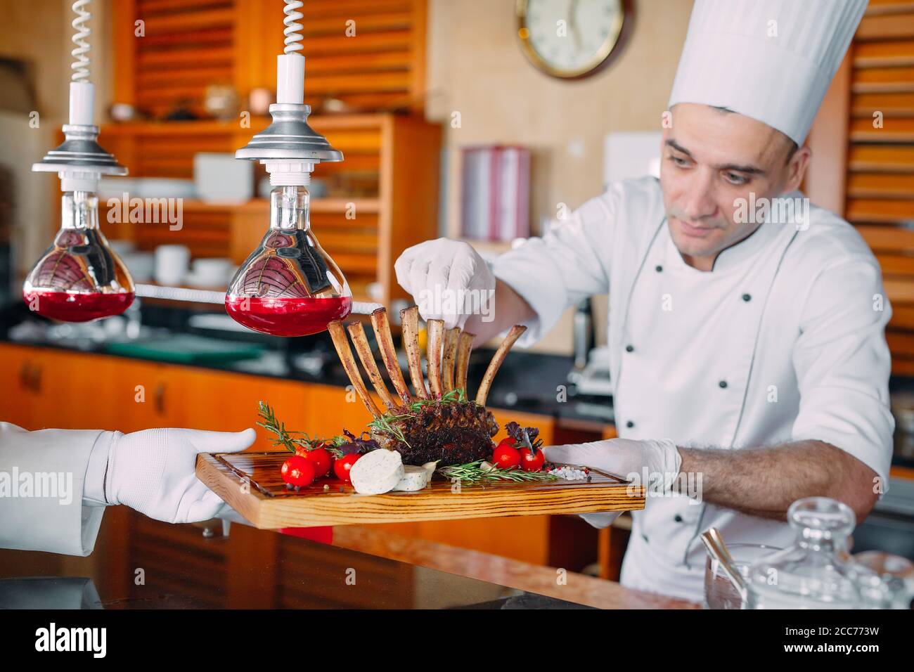 The cook passes the waiter the finished dish. rack of lamb Stock Photo ...