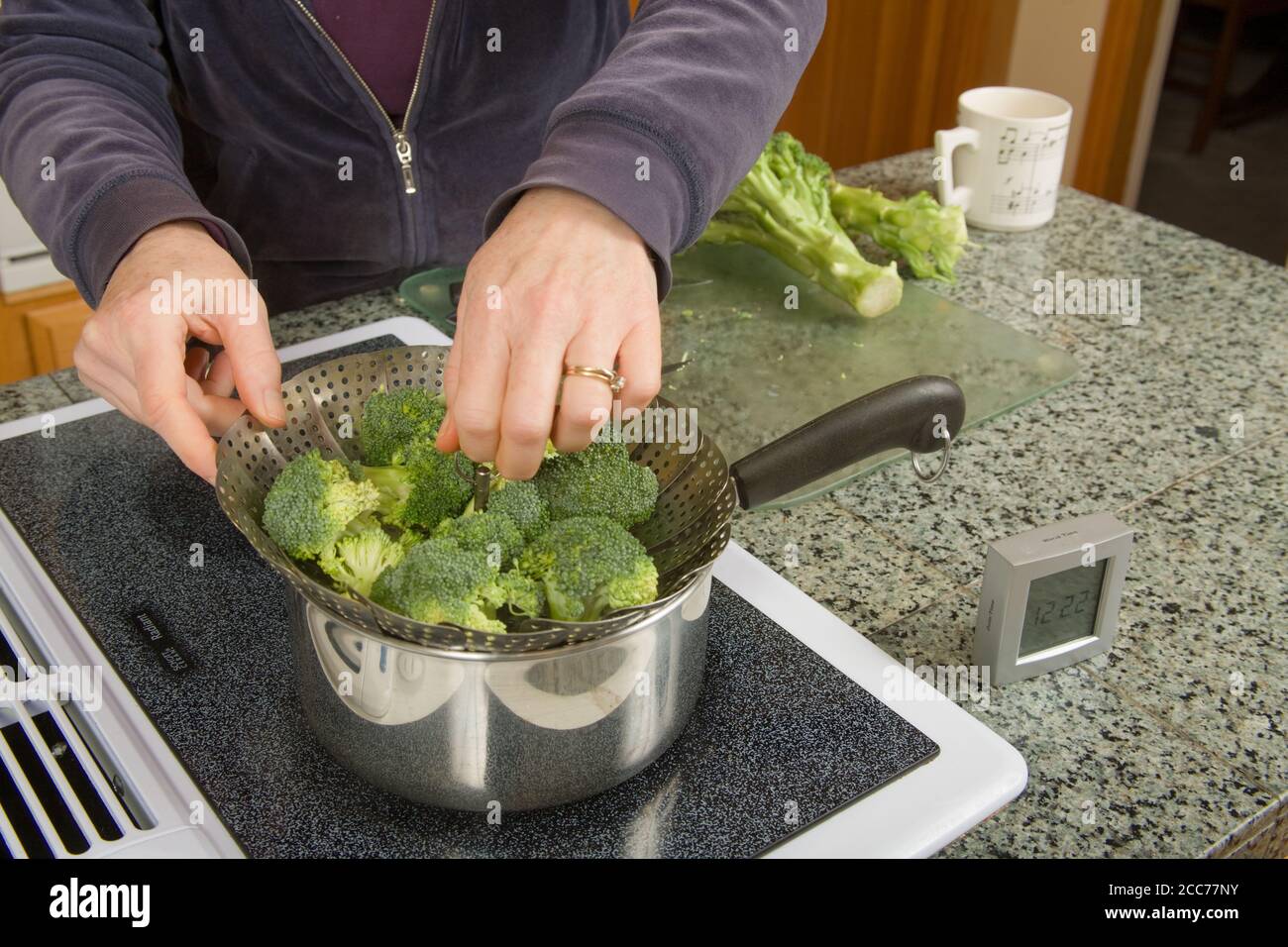 Placing a strainer of chopped broccoli into a pan to be blanched in ...