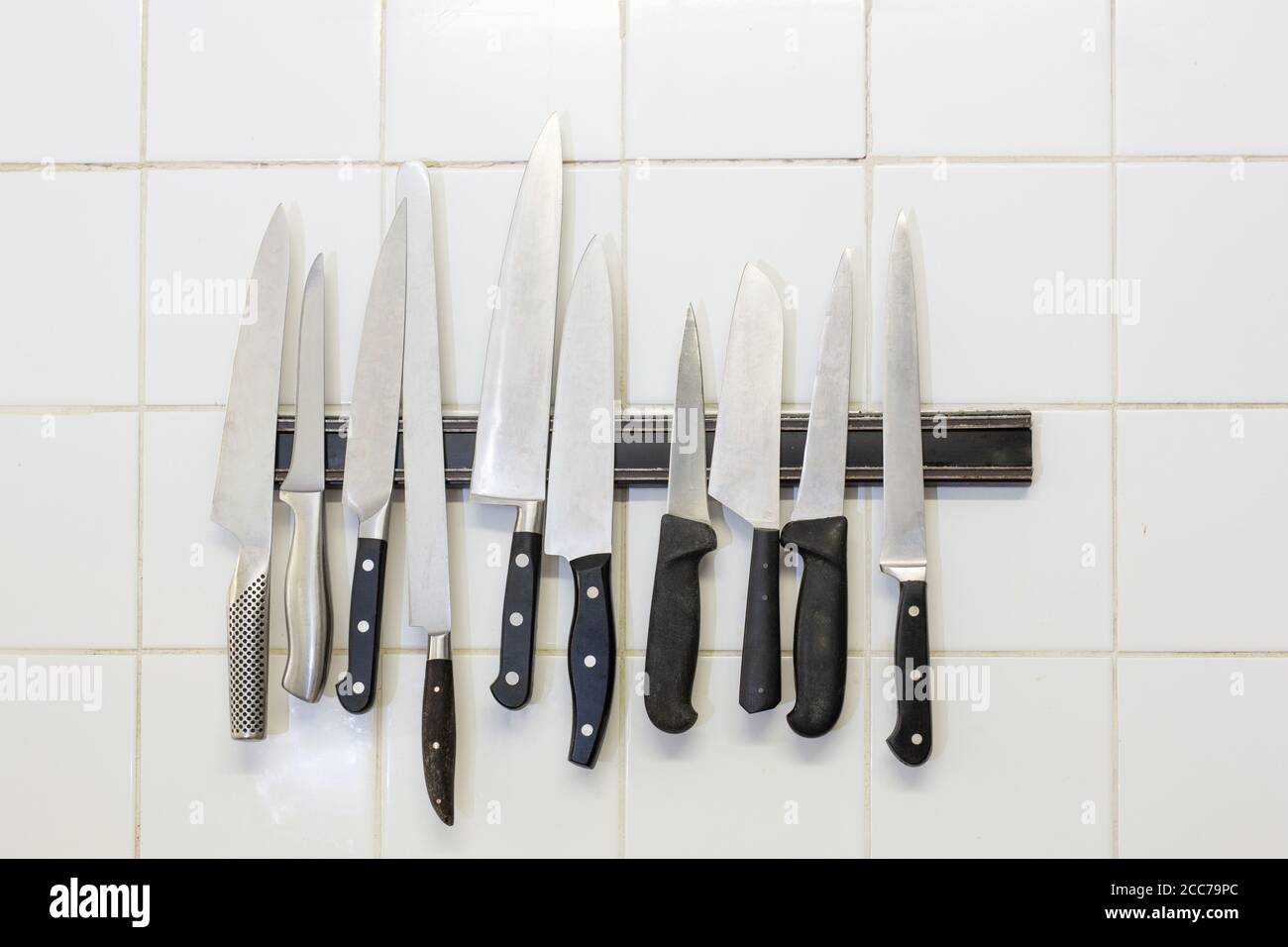 Collection of professional kitchen knives hanging on the wall with a ...