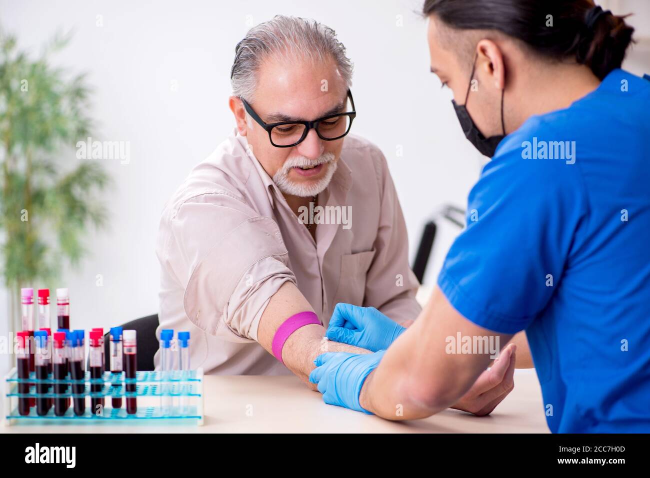 Old patient visiting young male doctor in blood transfusion concept ...