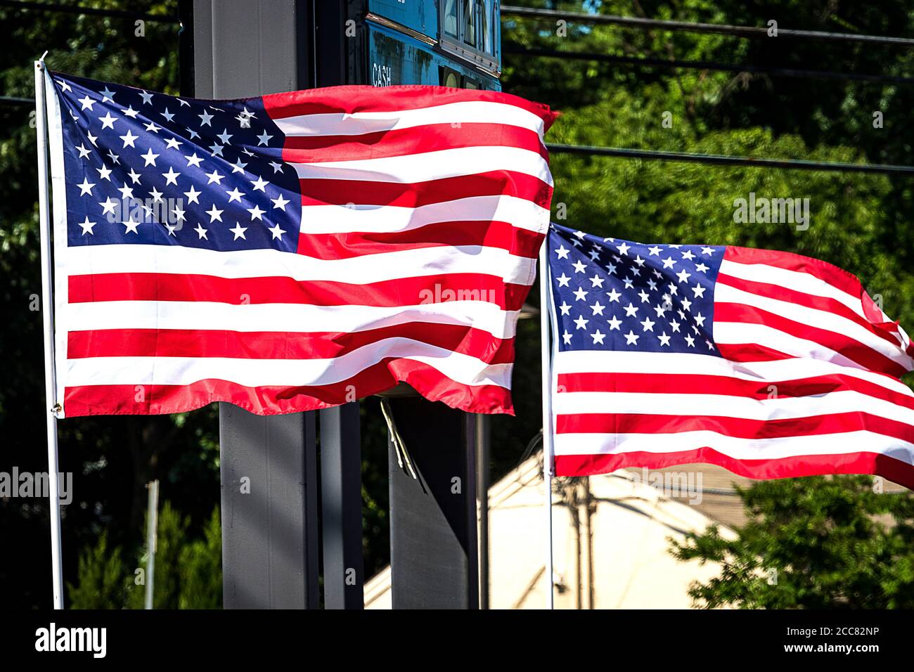 Two American flags wave vociferously in the wind in a suburban area ...