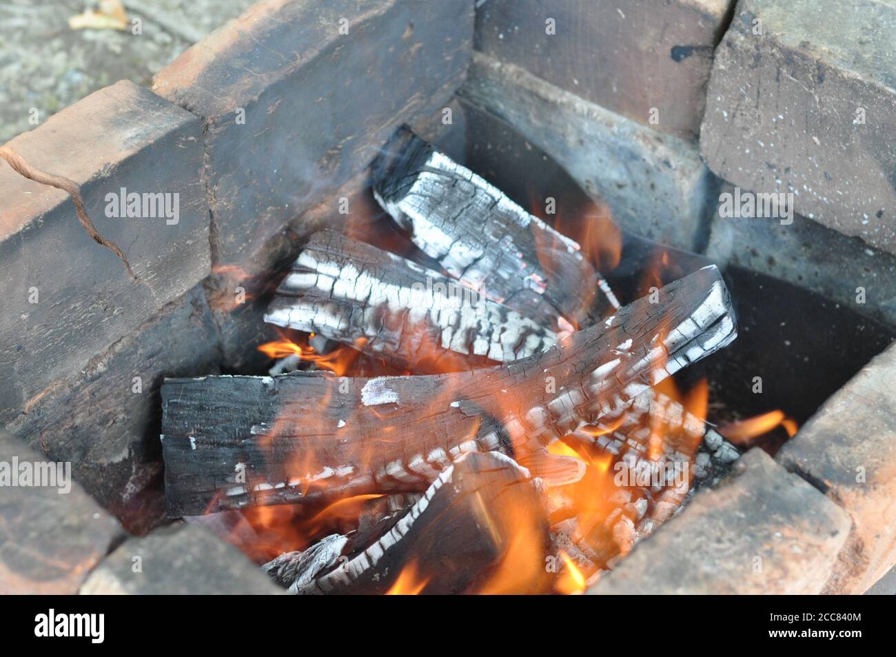 Burning firewood with flames over cracked logs covered with gray ashes ...