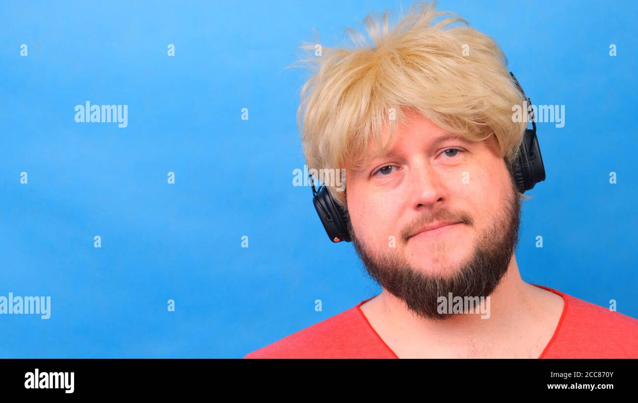 sad freaky fat man in a wig and a pink T-shirt in his hands listens to ...