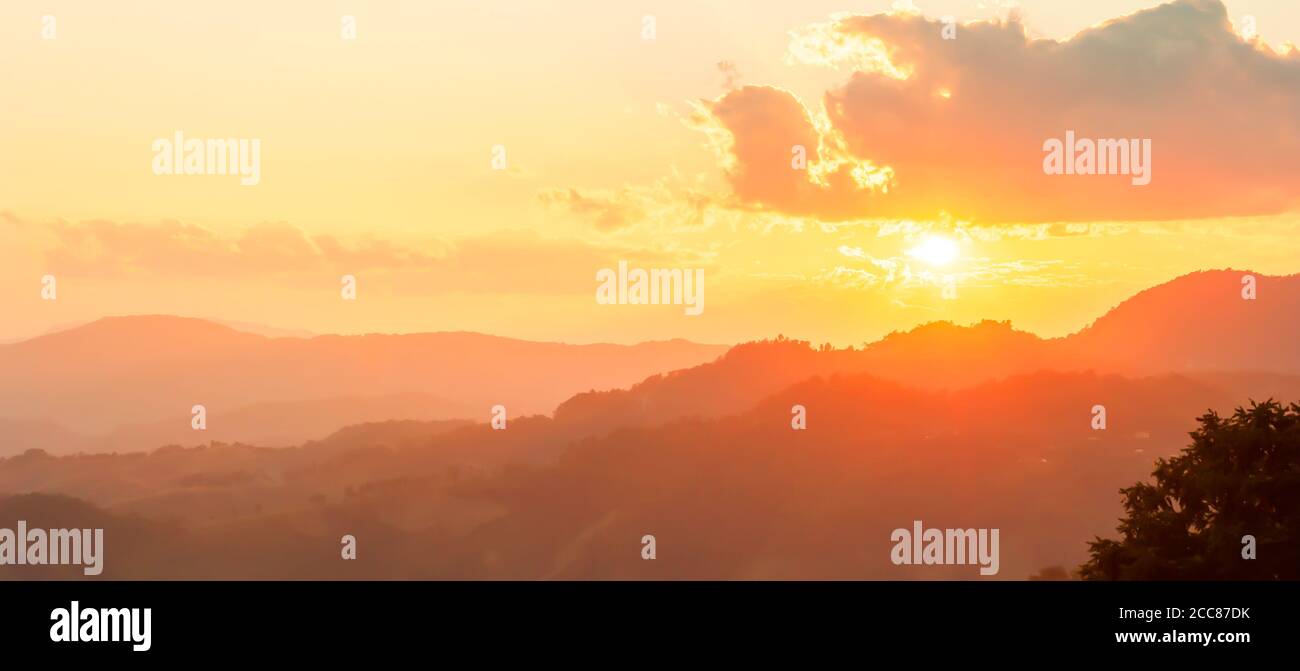 Panoramic mountain view at sunset, glowing sun setting behind dramatic ...