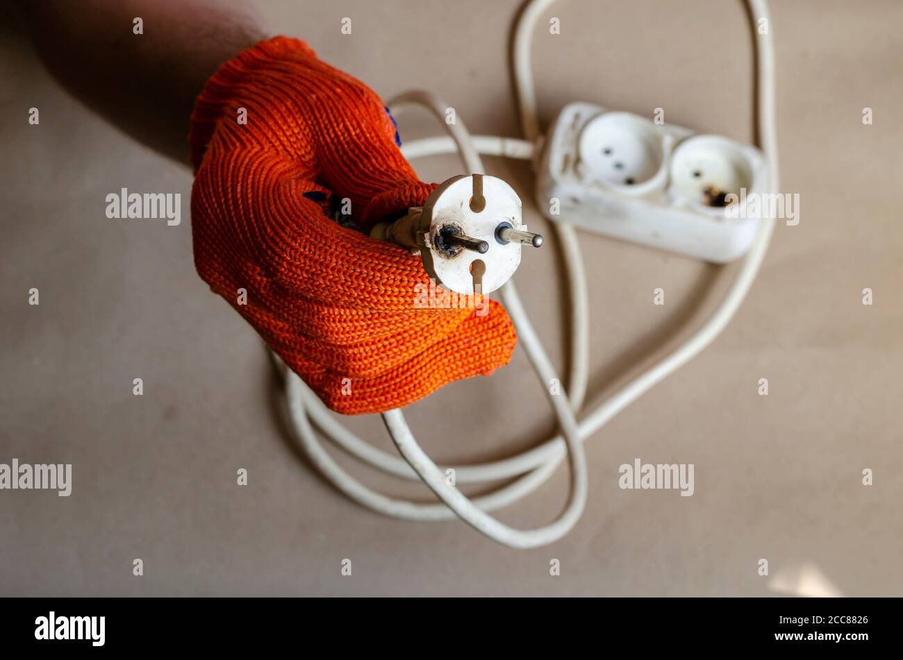 Hand wearing a protective orange glove holds an electrical plug after ...