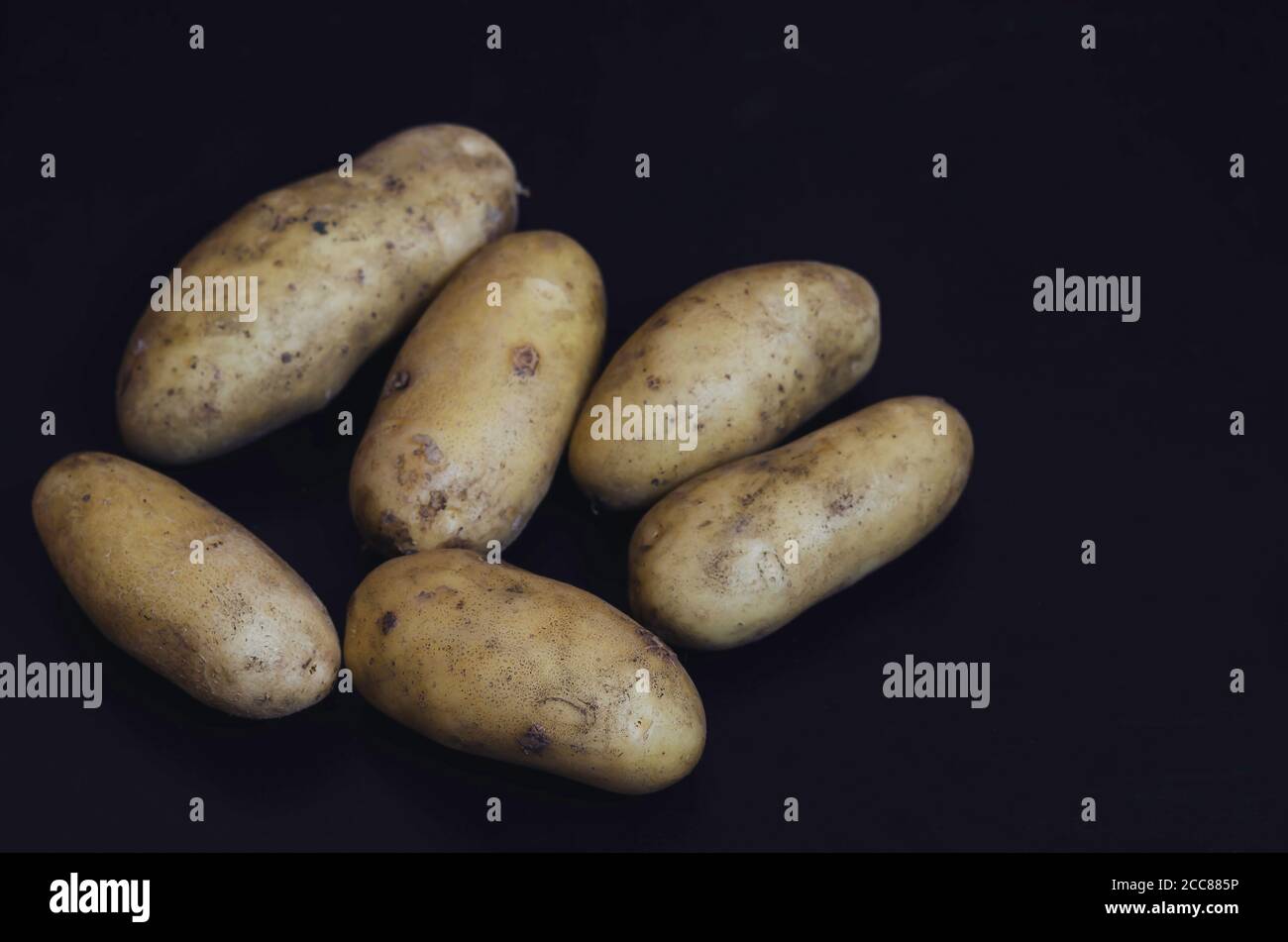 Raw potatoes in a peel on a black background. A portion of raw root ...