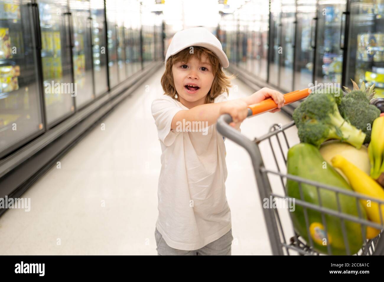 Joyful child boy in supermarket buys vegetables. Healthy food for ...