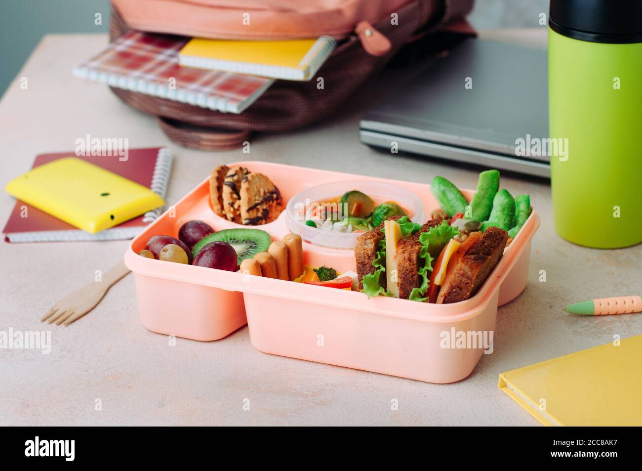 Open lunch box with healthy food on the table near backpack, laptop and ...