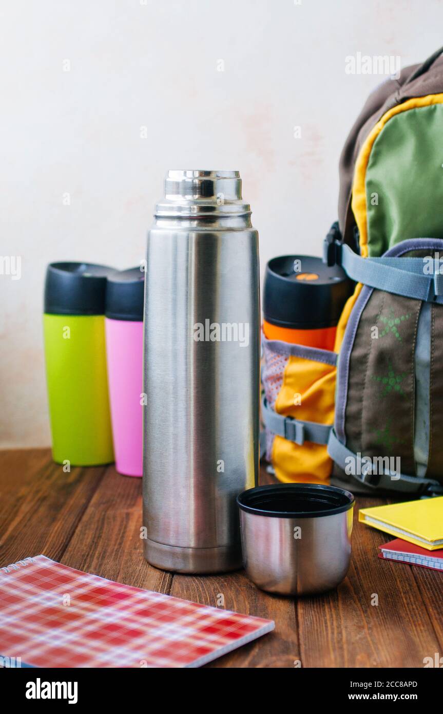 Open thermos bottle and color plastic thermos mugs on wooden background ...