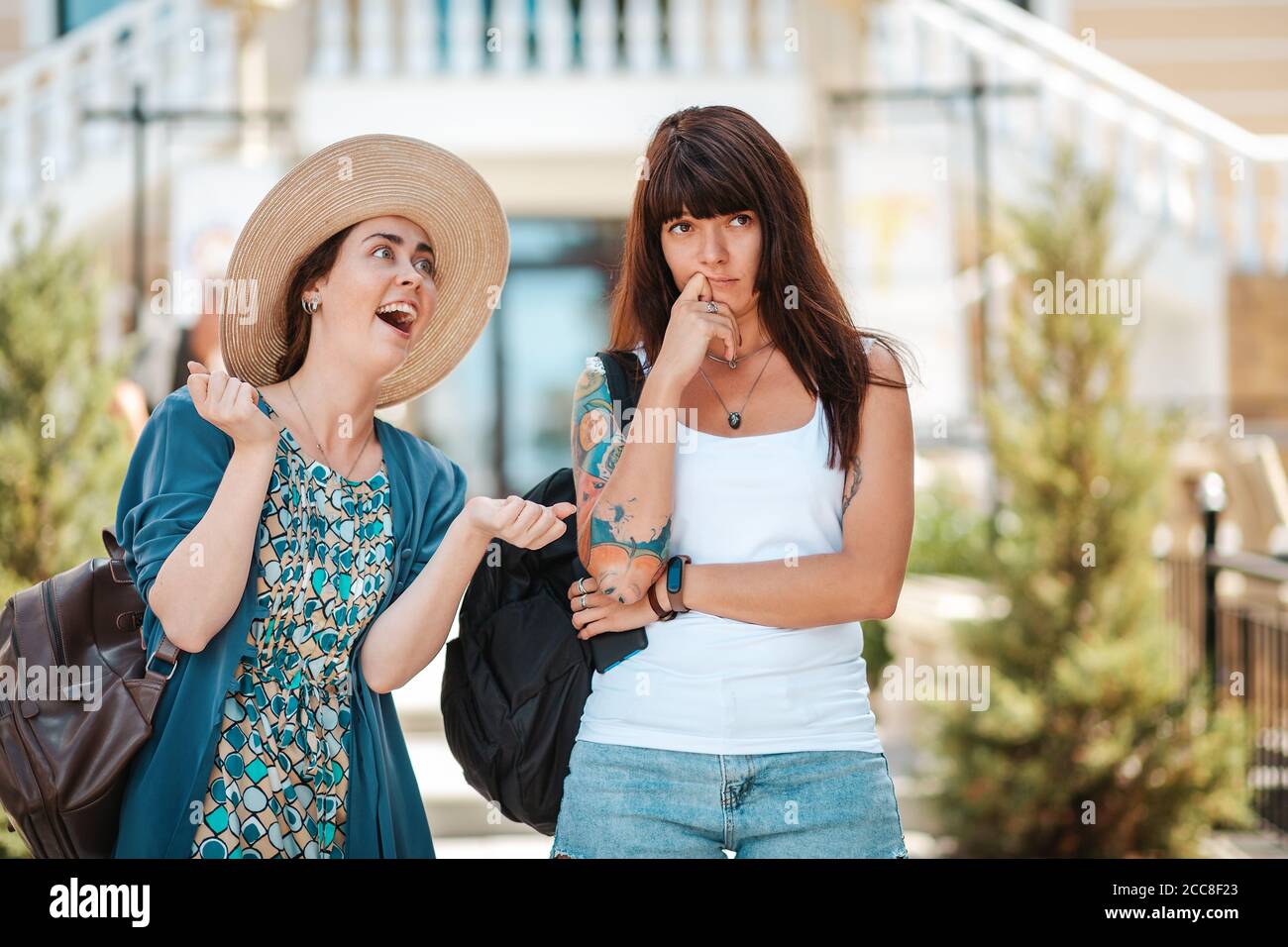 Portrait of a two young women chat on the street. One woman listens ...