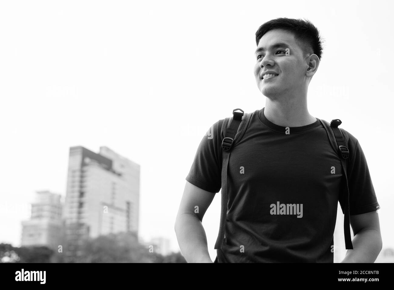 Young handsome Asian tourist man with backpack relaxing at the park ...