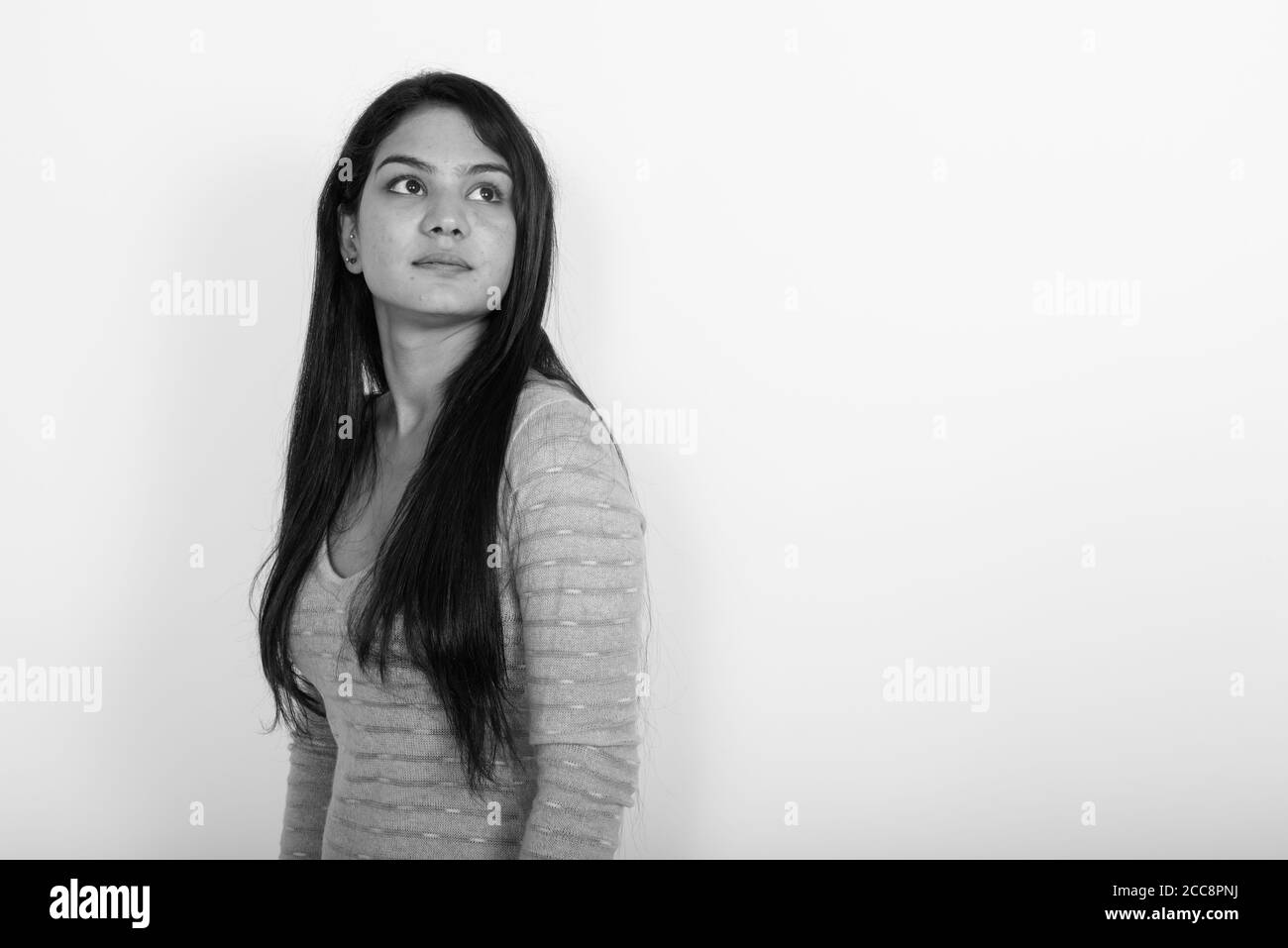 Studio shot of young Indian woman thinking while looking back against ...