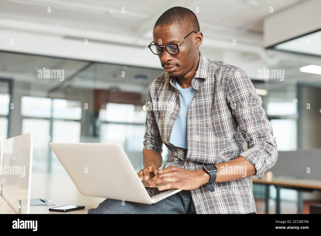 African young designer in eyeglasses typing on laptop computer he ...